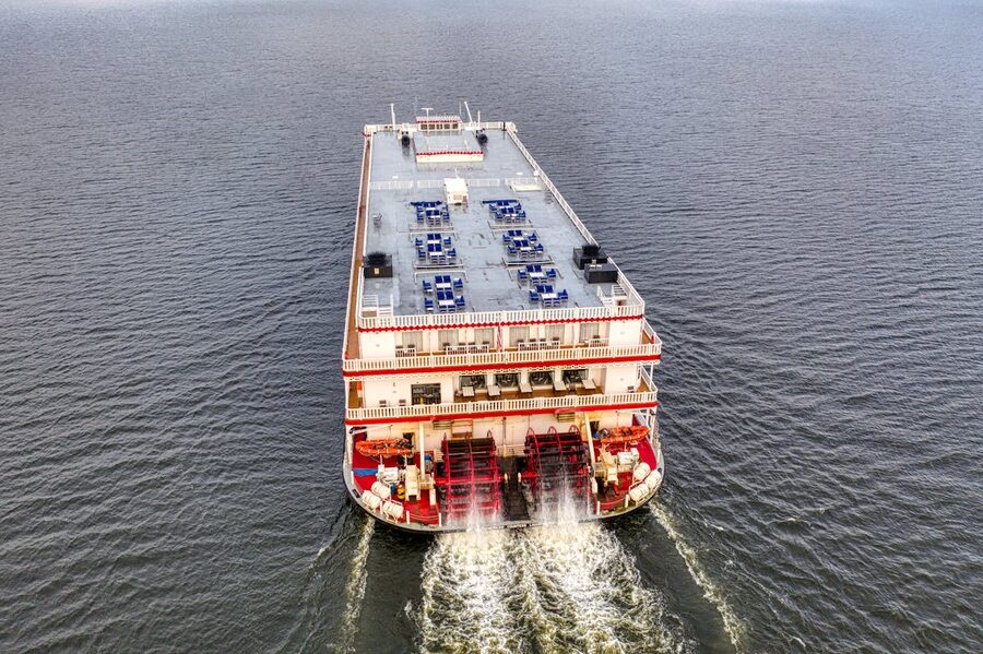 Aerial shot of a red and white paddle steamboat cruising on a wide river