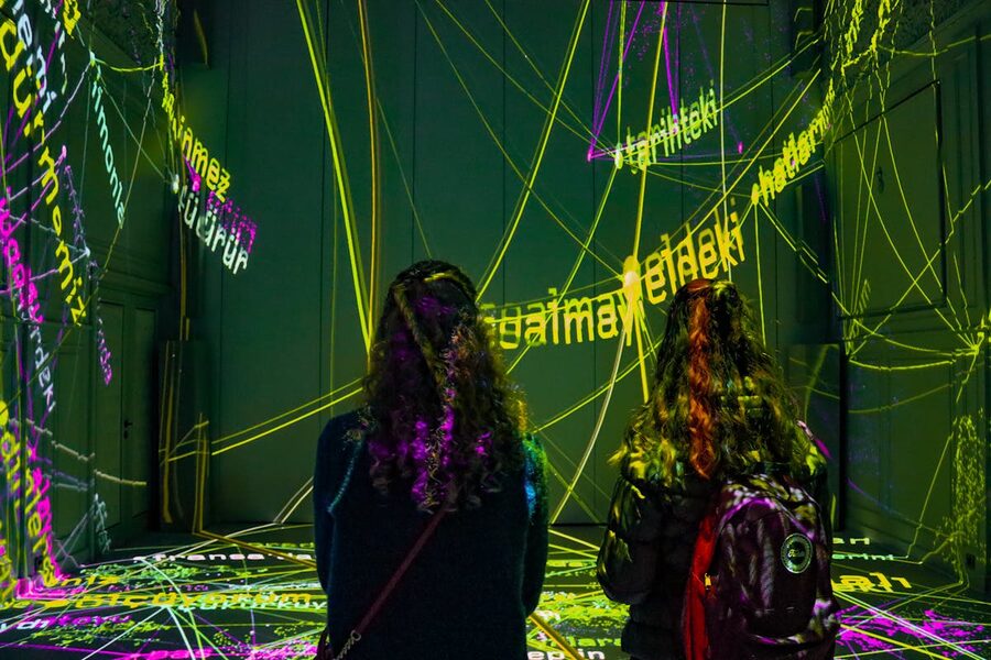 Two women observing text projection art installation dark room