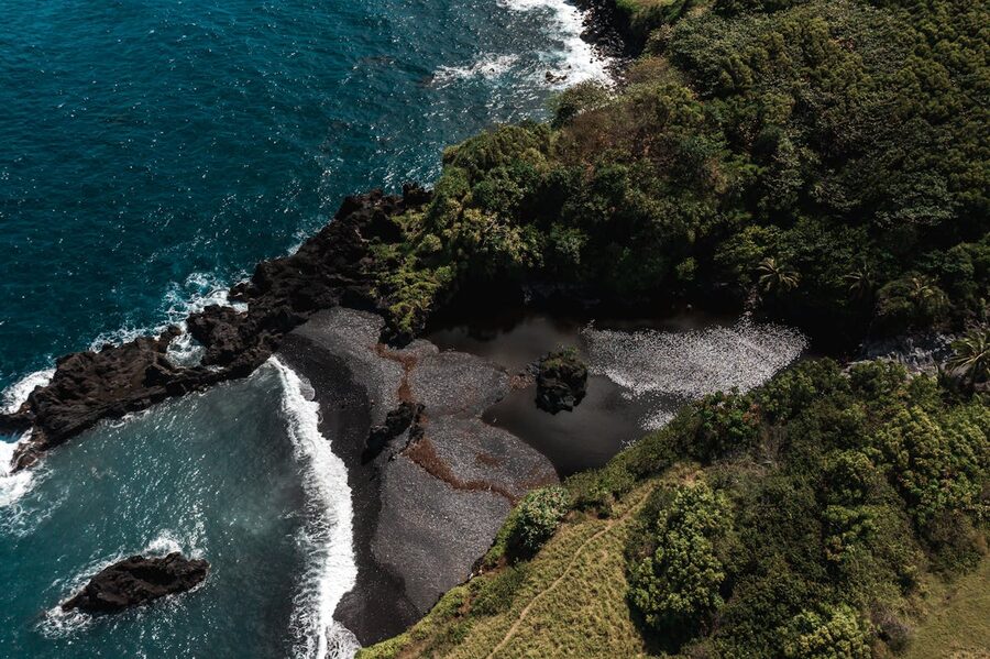 Aerial shot of black sand beach surrounded by greenery in Hana Maui
