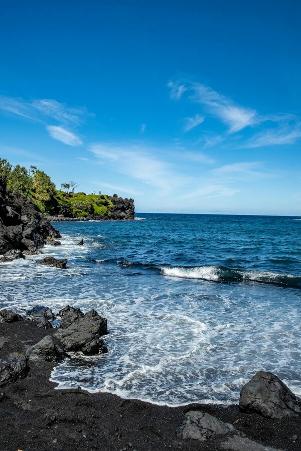 Black sand beach with clear blue sky and ocean in Hana Hawaii