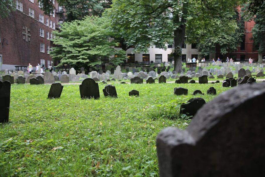 Weathered tombstones in a historic Boston cemetery, green grass and old slate markers