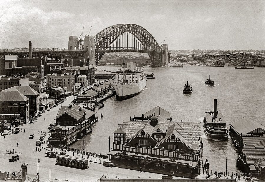 Black-and-white photo of Sydney Harbour Bridge nearly complete in 1931 with ferries at Circular Quay