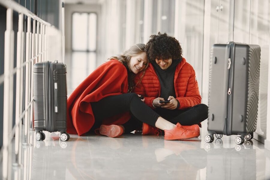 Couple sitting on airport floor with luggage checking phone at Cancun arrival