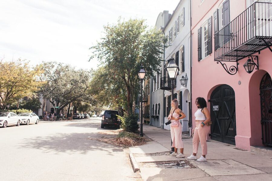 Two women walking on a pastel-colored Charleston street south of Broad