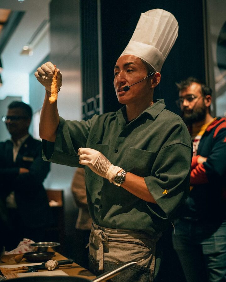 Chef wearing hat demonstrates cooking techniques to an audience