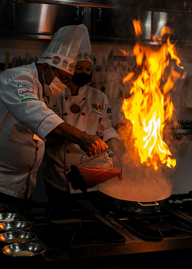 Chefs in uniform creating a flambe dish over intense flame in a restaurant