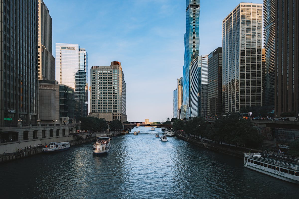 View of Chicago River flanked by modern skyscrapers with boats cruising under a clear blue sky