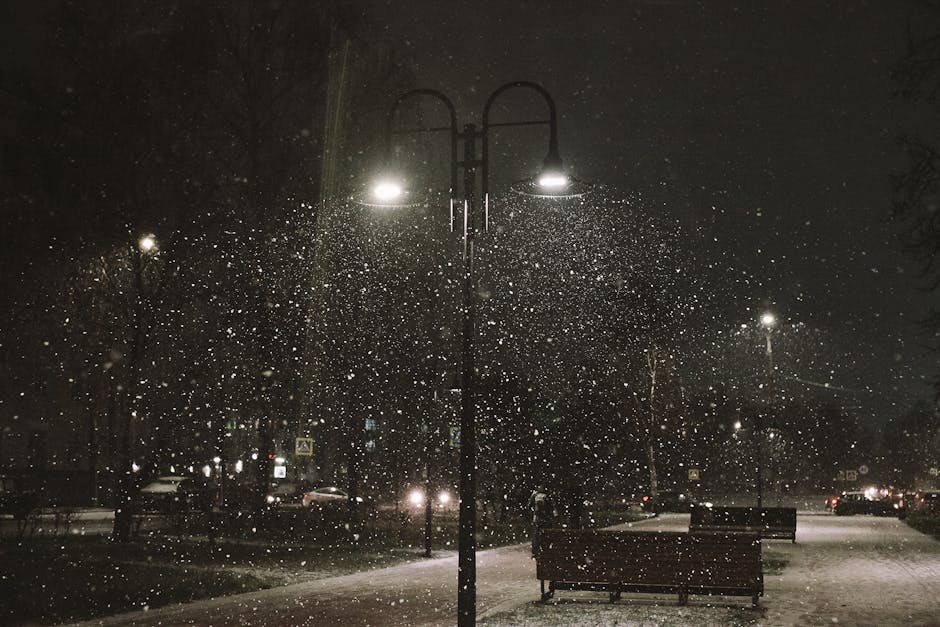 Nighttime city street with snow falling under streetlights