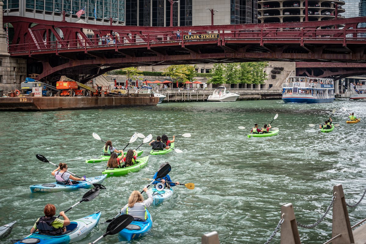 Group of kayakers paddling under Clark Street Bridge in Chicago with urban skyline