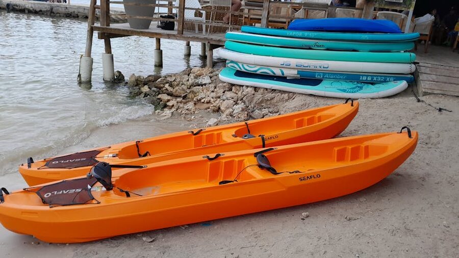 Orange kayaks and stacked paddleboards on a sandy beach