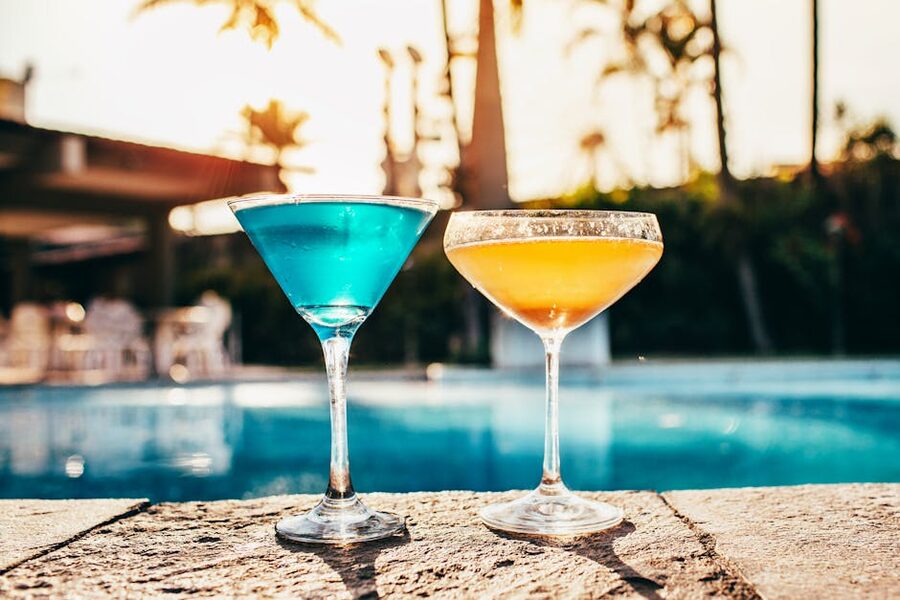 Two tropical cocktails on a low table by a swimming pool at golden hour