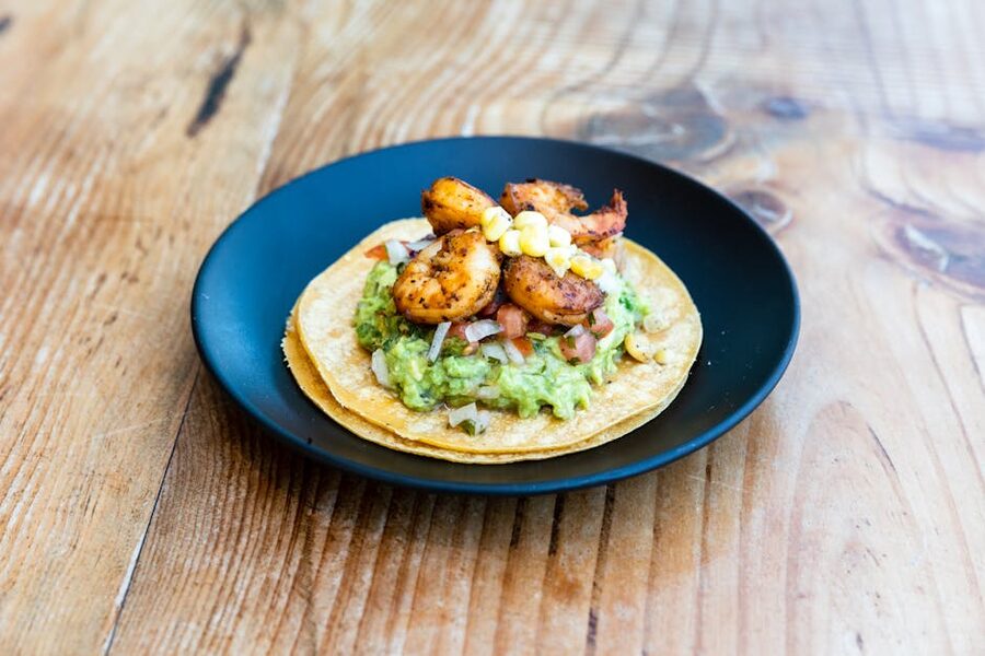 Three shrimp tacos with guacamole and corn on a wooden board
