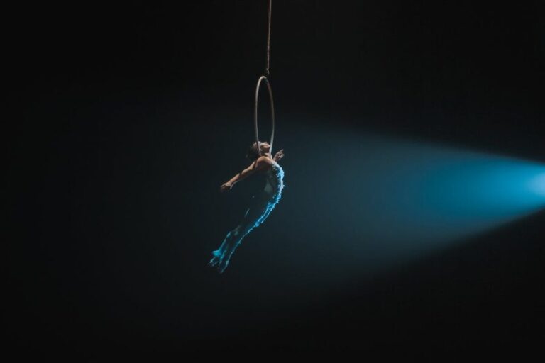 Aerial artist performing on hoop illuminated against dark background