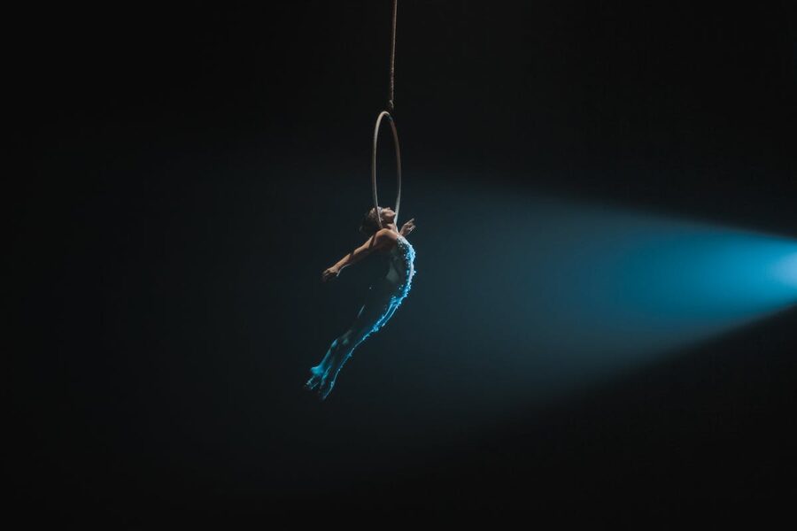 Aerial artist performing on hoop illuminated against dark background