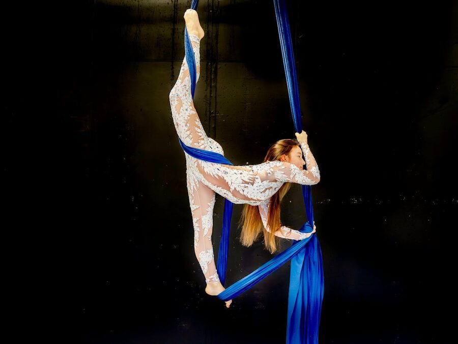 Aerialist performing on blue silk against dramatic backdrop