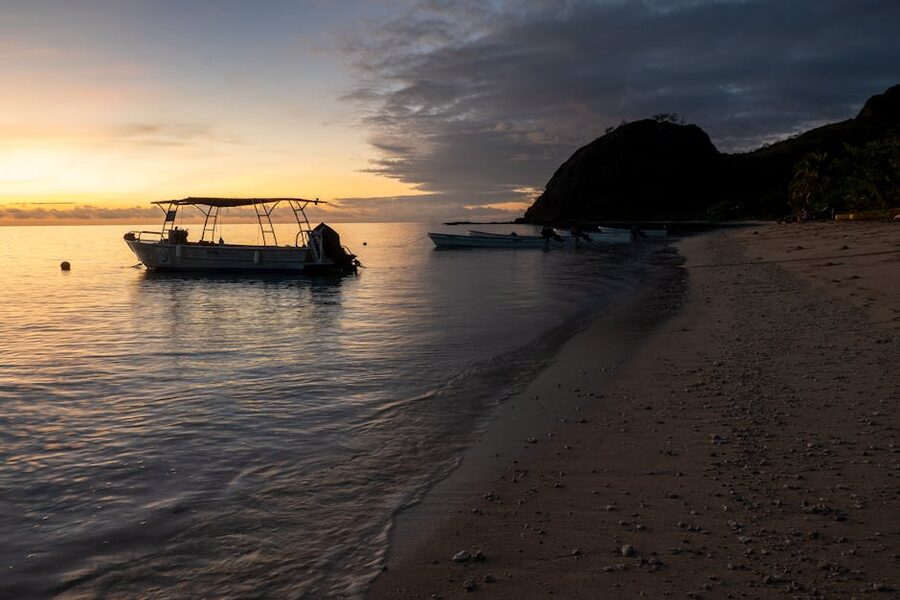 Tranquil Fijian beach at sunrise with boats