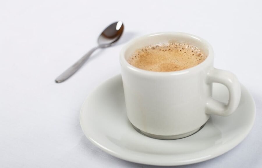 A small white cup of frothy Cuban coffee