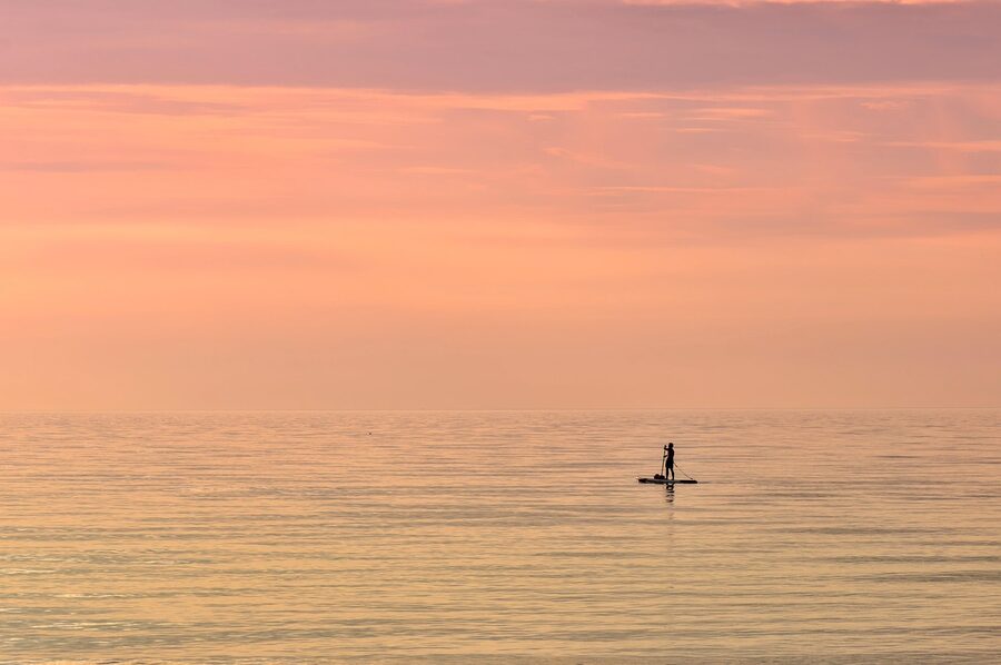 Silhouette of a paddleboarder at sunset on calm water