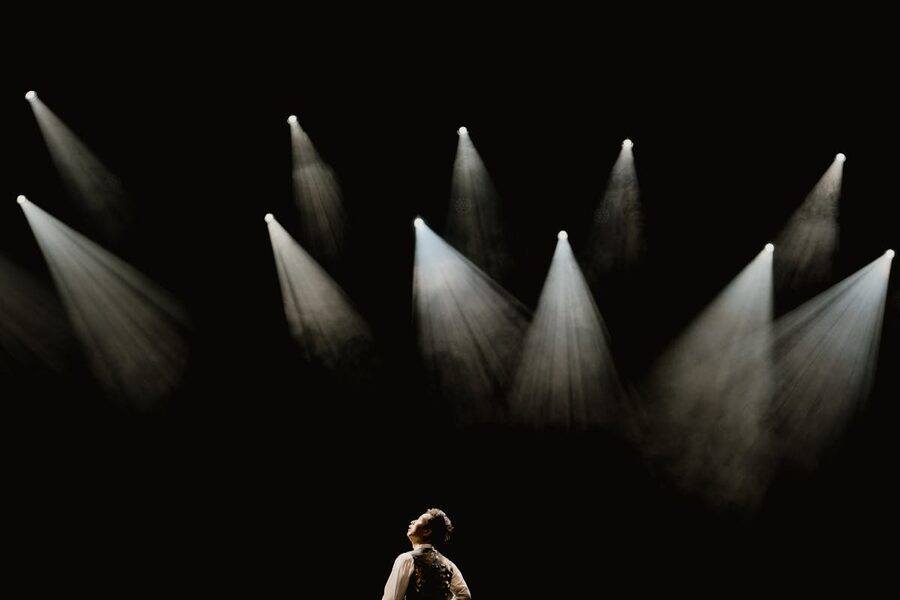 Solo performer standing in spotlight on dark stage