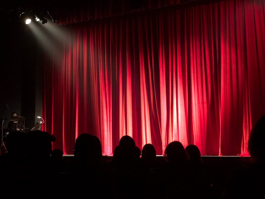 Theater stage with red curtains and audience silhouettes