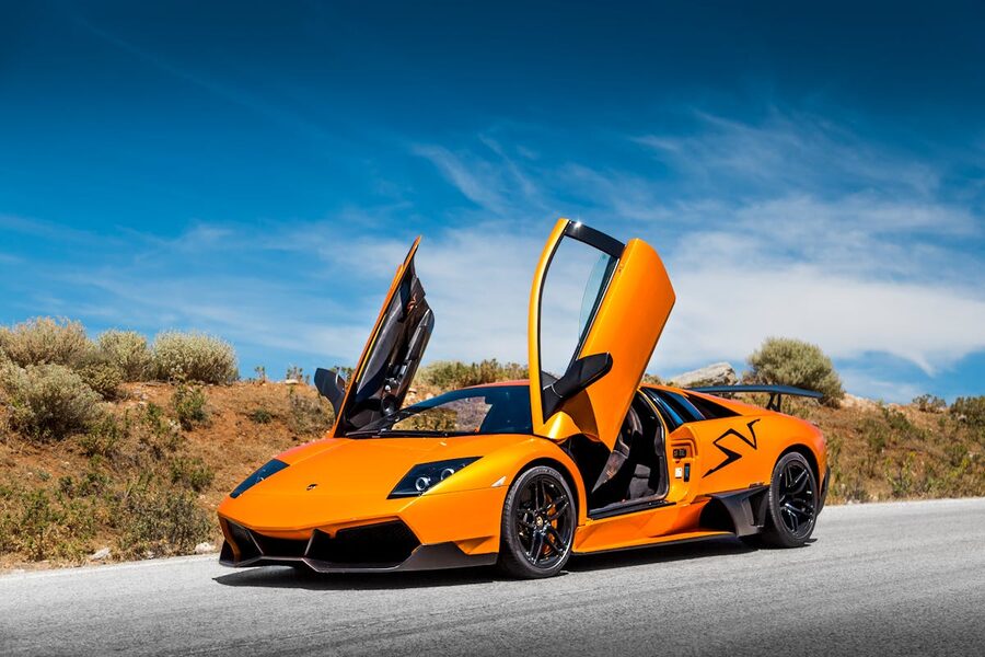 Orange supercar with doors open under bright blue sky