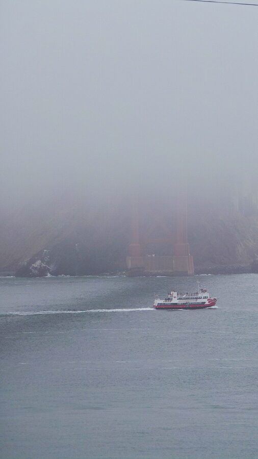 Ferry boat passing under the Golden Gate Bridge on a foggy day in San Francisco