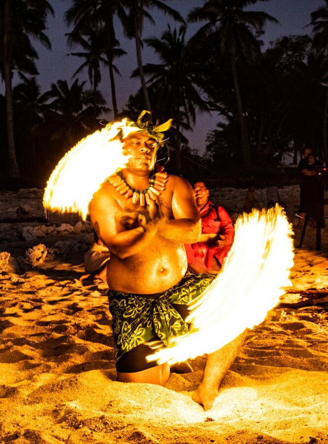 Fire dancer performing on a tropical beach at night surrounded by torches