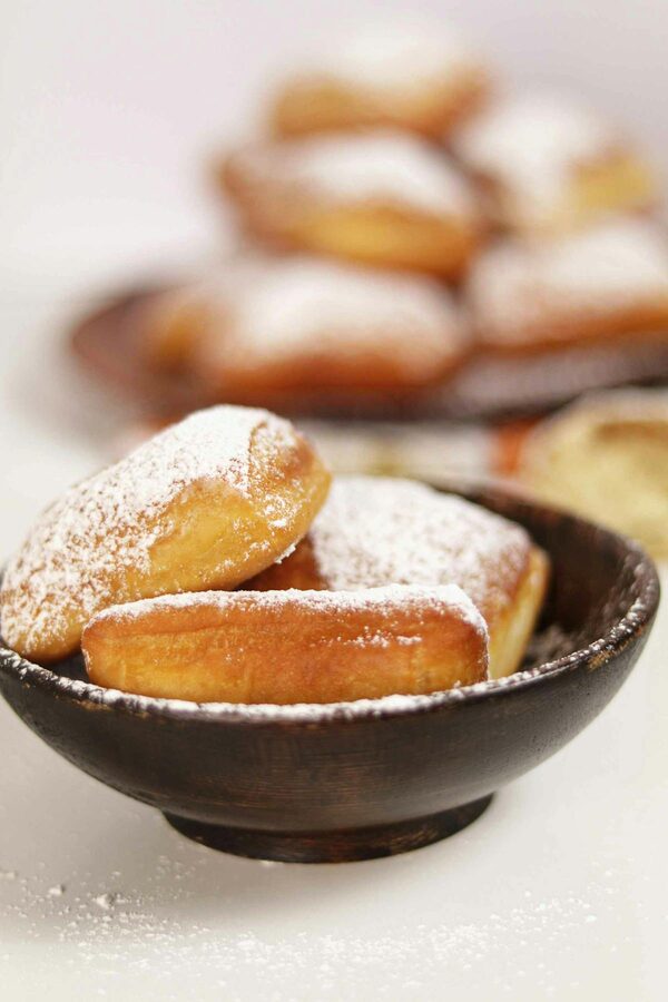 Close-up of freshly made beignets dusted with powdered sugar in a wooden bowl