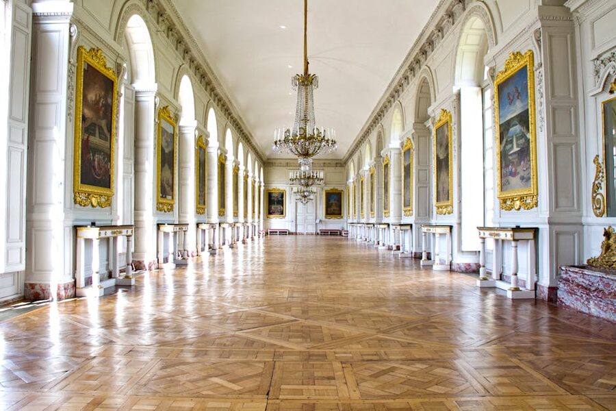 Luxurious hallway of the Grand Trianon in Versailles with ornate chandeliers and golden framed paintings