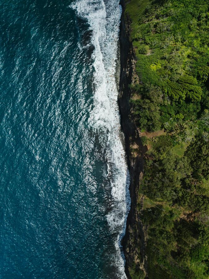 Aerial photograph of Hawi coastline with ocean waves meeting green cliffs
