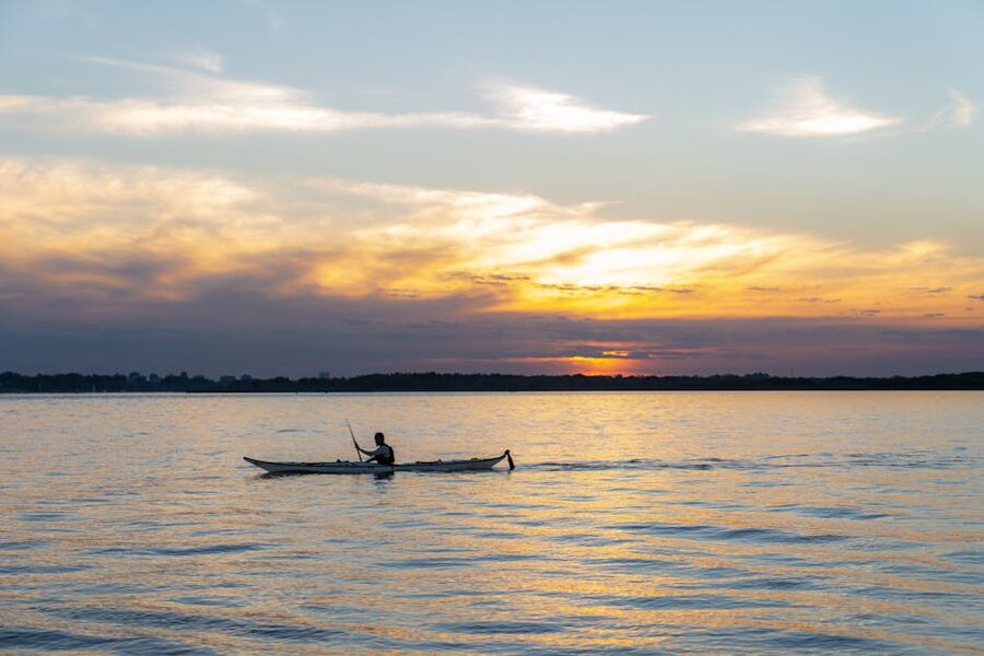 A kayaker paddling toward the sunset on calm ocean water