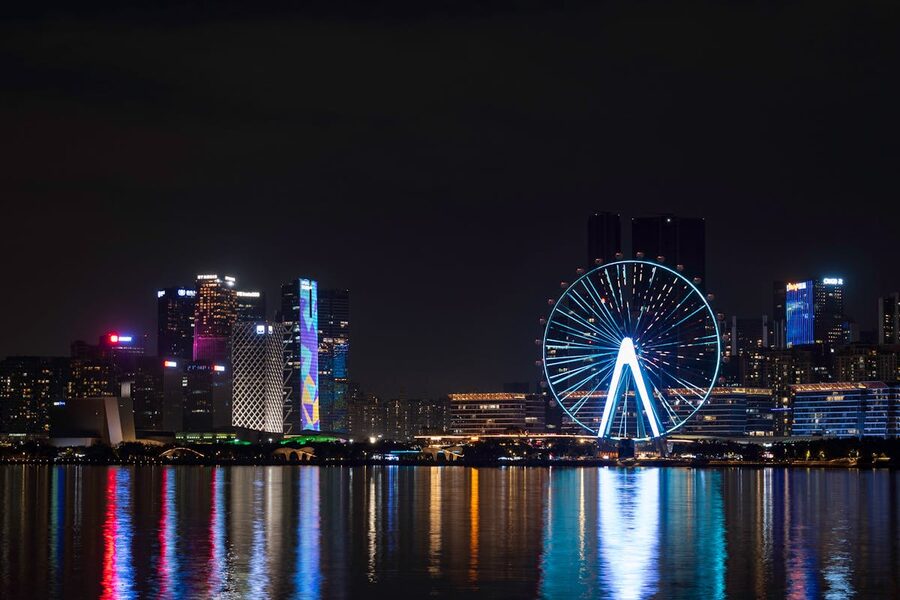 Illuminated ferris wheel and city skyline reflecting on water at night