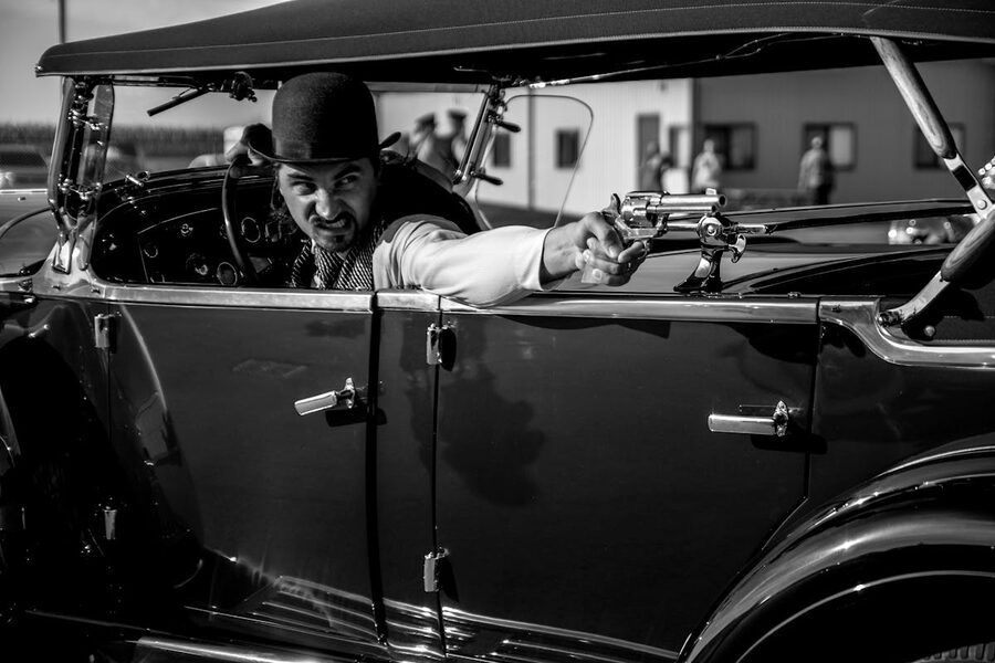 Man in vintage car aiming revolver 1930s gangster style black and white