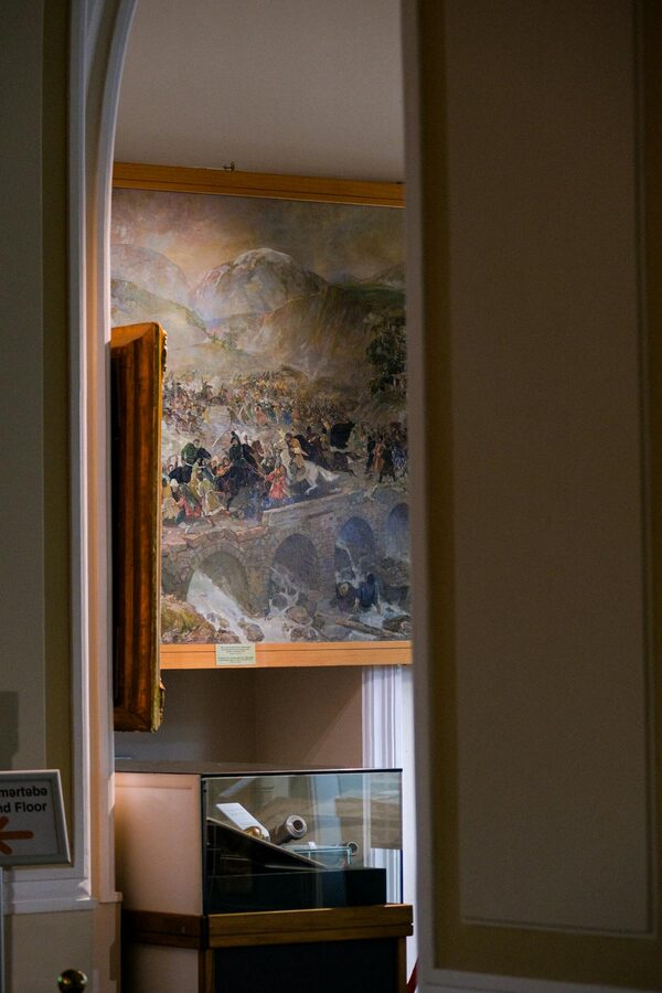Interior of a museum room showcasing historical painting and display cabinets
