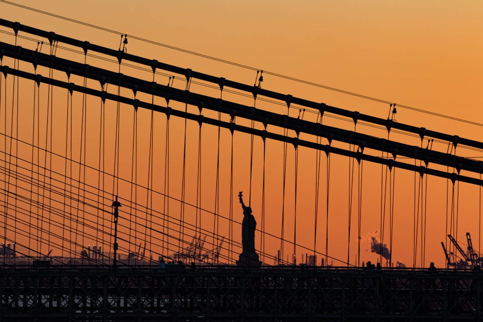Statue of Liberty silhouetted through bridge cables at sunset