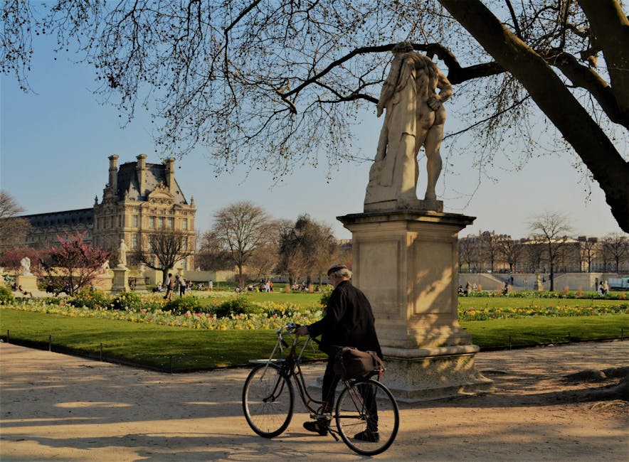 Cyclist passing a statue in the Tuileries Garden with the Louvre behind