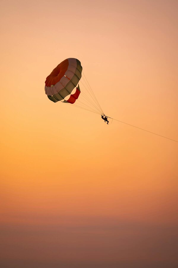 Silhouette of a parasailer soaring against a vivid sunset sky