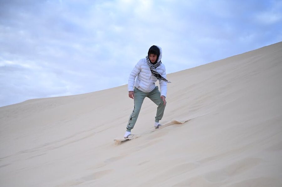 Person sandboarding down a steep sand dune