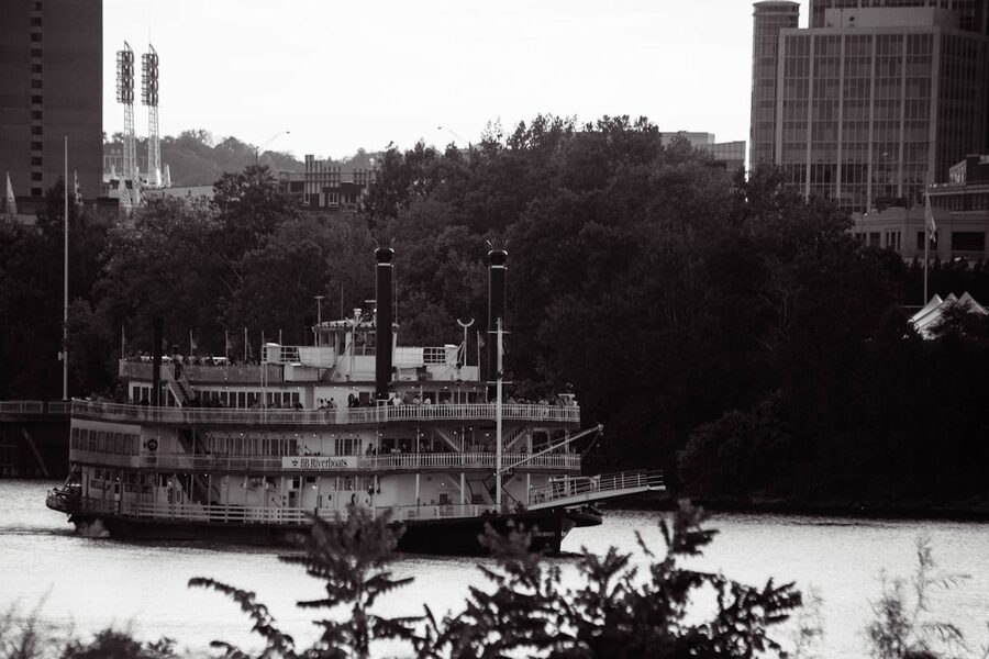 Traditional riverboat sails along a river with city skyline and trees