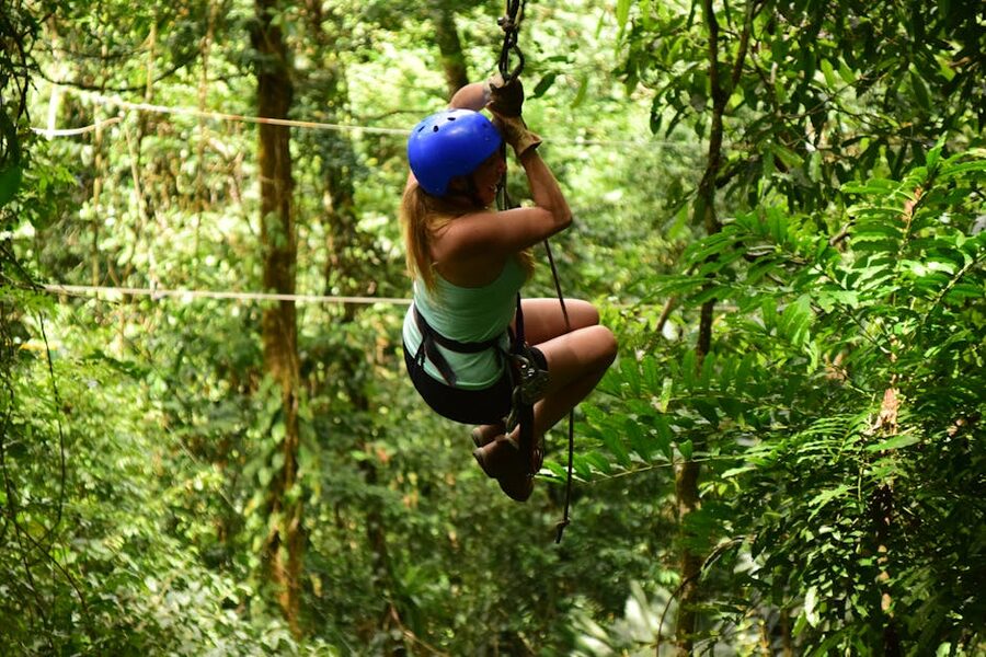 Woman ziplining through a lush forest with arms outstretched