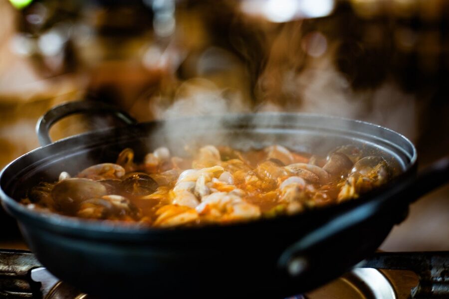 Seafood stew bubbling in a black pot with steam rising