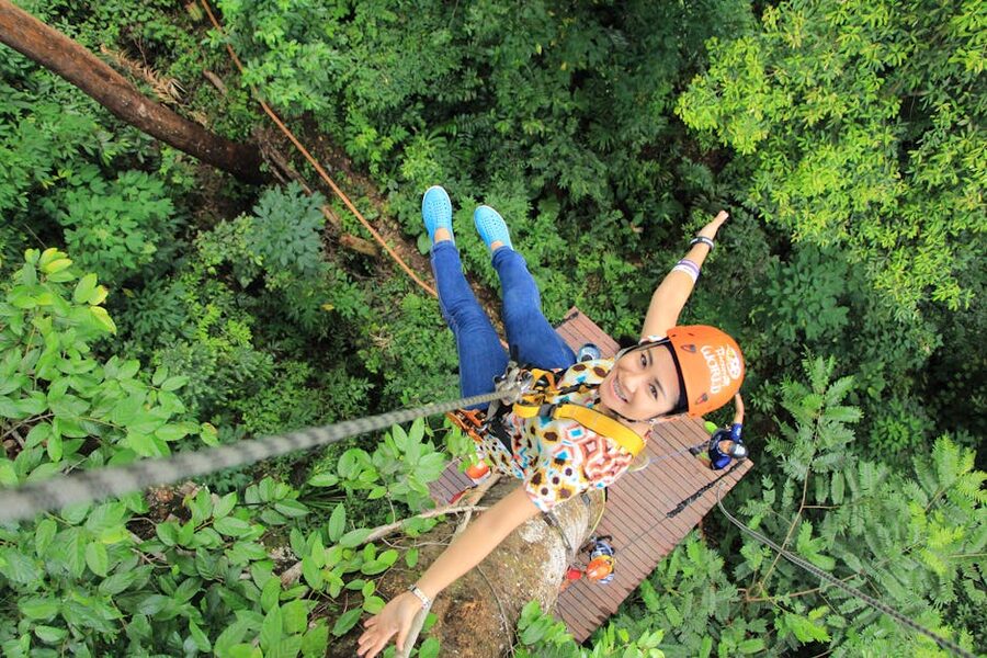 Zipline rider in orange helmet through forest canopy