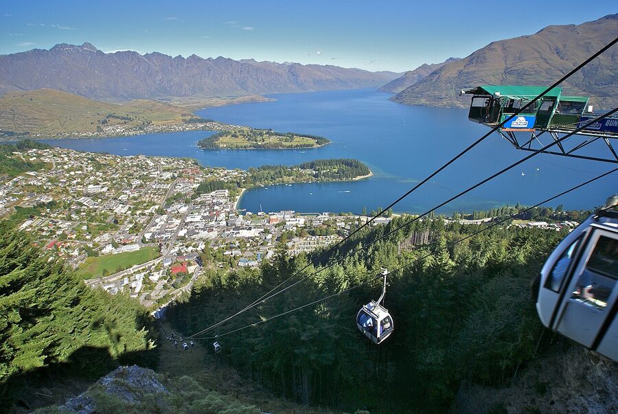 Skyline gondolas climbing past forested cliffs over Queenstown