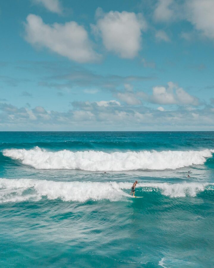 Surfer riding a wave on North Shore Beach Oahu under bright blue sky
