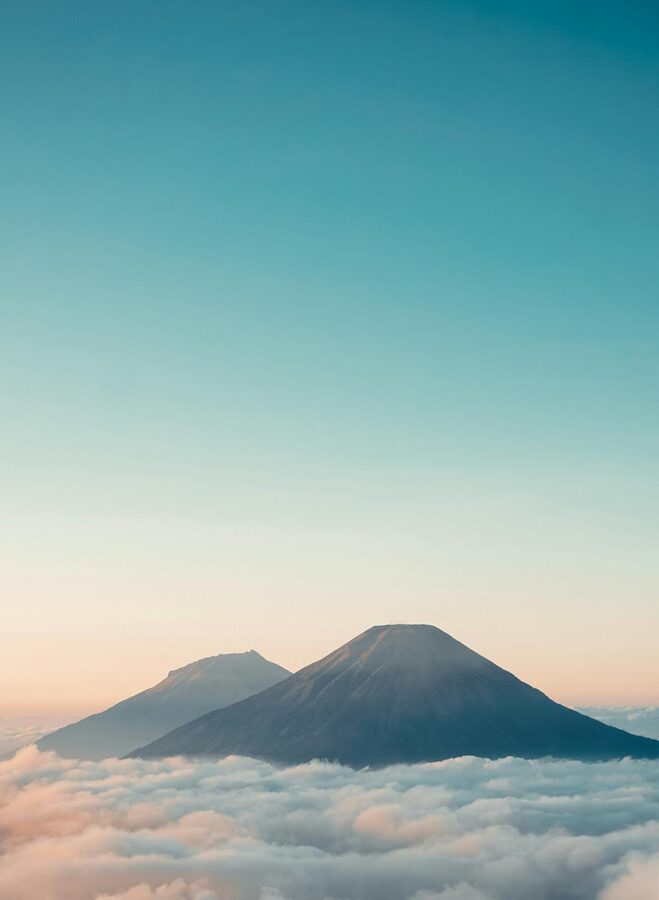Aerial view of volcano rising above a sea of clouds under clear sky