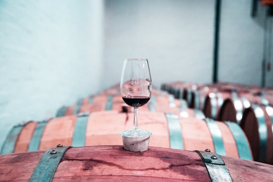 A glass of red wine resting on an oak barrel in a cellar