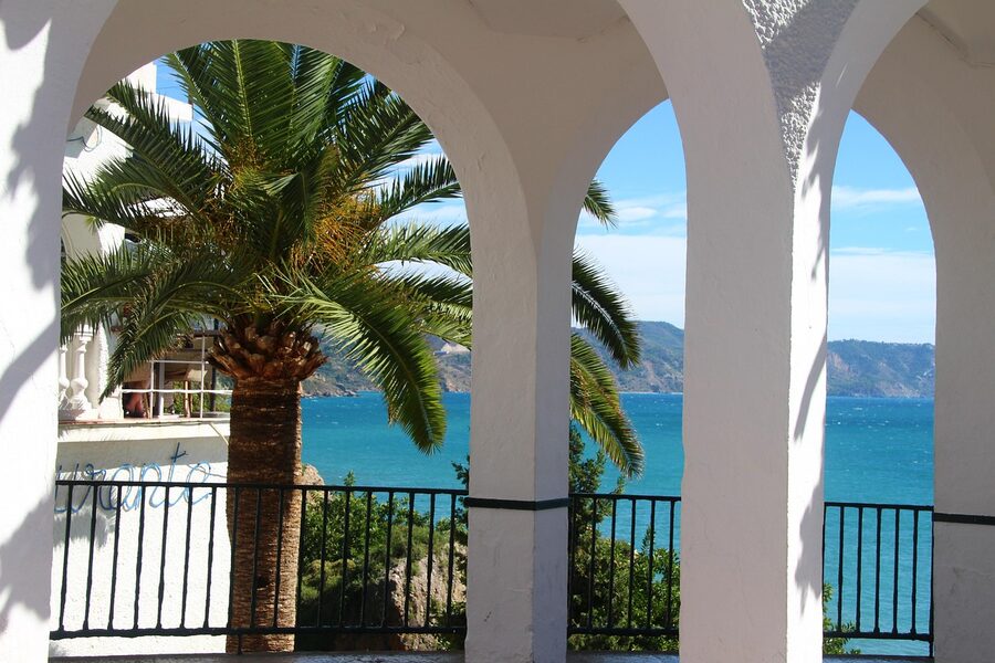 White columns of the Balcón de Europa with palm tree and Mediterranean sea view