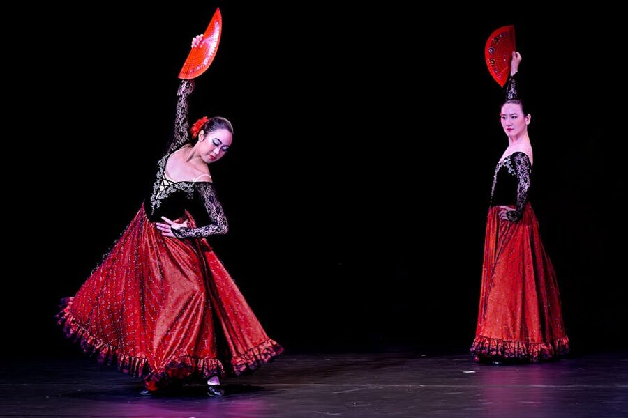 Two flamenco dancers performing with red fans on a Madrid tablao stage