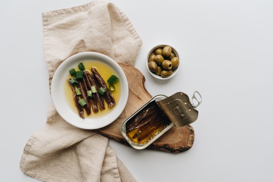 Anchovies in oil with green olives on a rustic wooden board