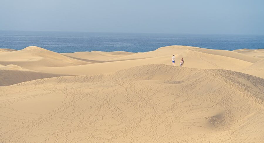 Maspalomas Dunes from above with two figures crossing the sand and ocean in the distance